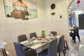 Uma sala de jantar com uma mesa comprida posta para seis pessoas, rodeada por cadeiras, com um quadro de um cais na parede.