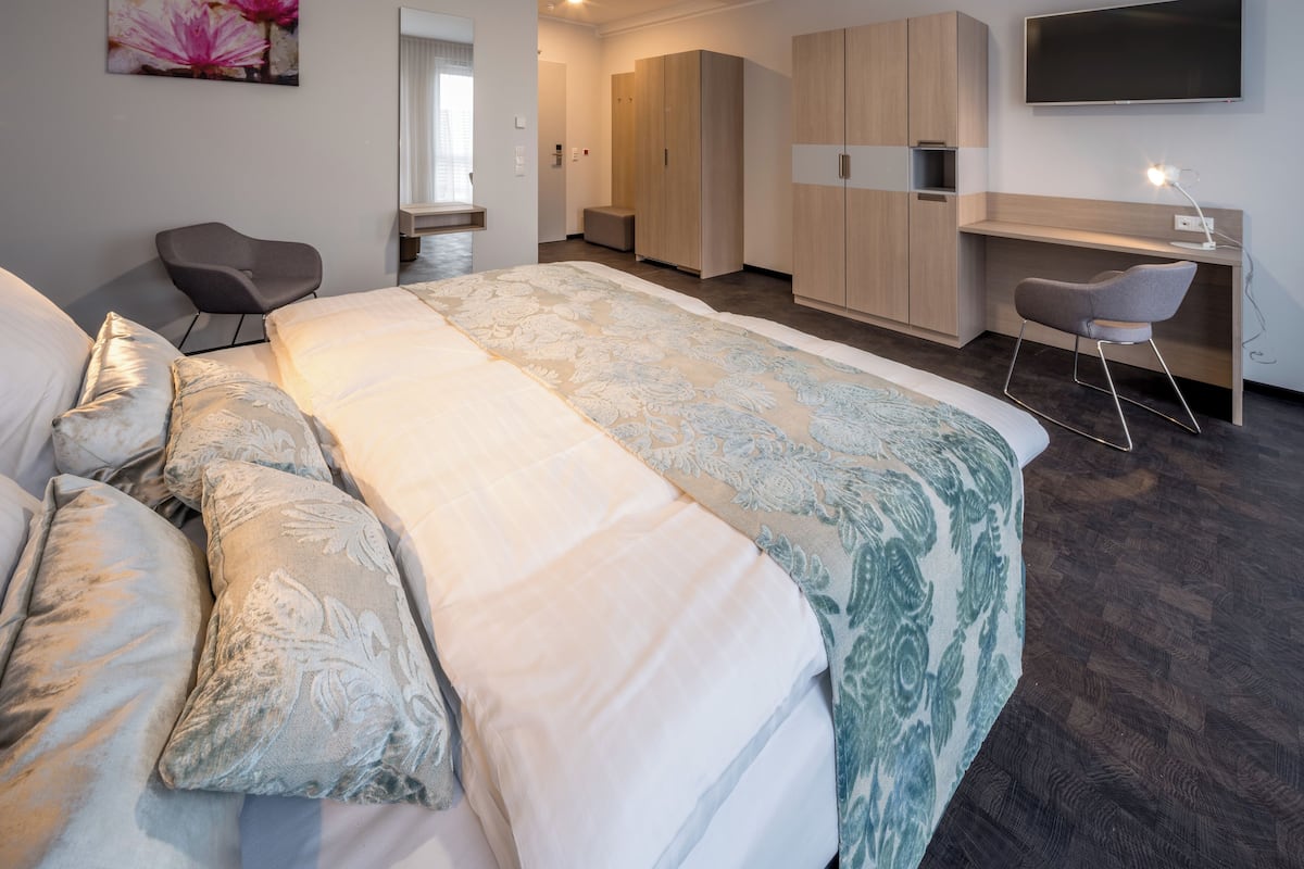 Quarto de hotel moderno com uma cama grande, uma escrivaninha e uma televisão.