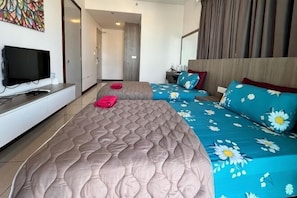 Quarto de hotel com duas camas, televisão, escrivaninha e banheiro.