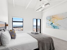 Quarto moderno com uma cama grande, vista da cidade pela janela e uma pintura abstrata grande na parede.