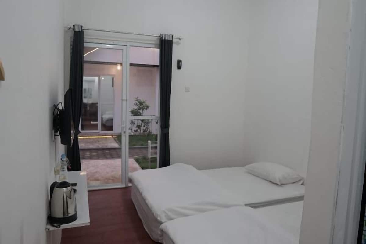 Quarto com duas camas, cafeteira, mesa pequena e porta de correr de vidro que dá para uma área externa.