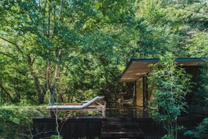 Uma cabana de madeira com varanda e uma cadeira de descanso, rodeada por uma floresta densa.