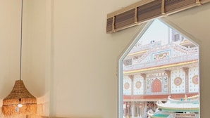 Quarto com cama, luminária pendente e janela com vista para um edifício tradicional.