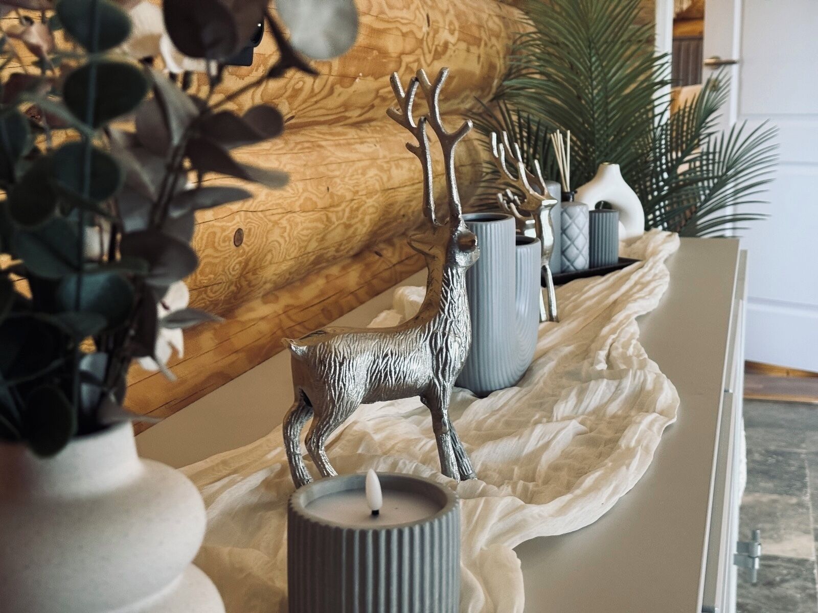 Uma prateleira decorativa com uma estatueta de veado metálico, uma vela e vários vasos.