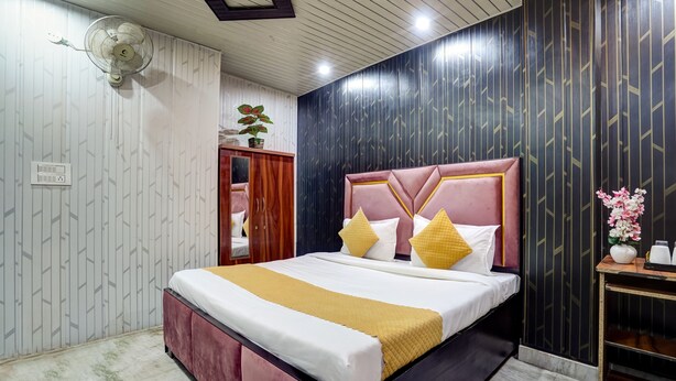 Quarto com cama, mesa de cabeceira, ventoinha na parede e planta em vaso.