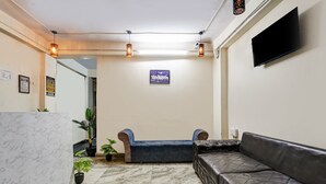 Uma área de recepção com balcão de mármore, um sofá azul, um sofá de couro preto e uma TV fixada na parede.