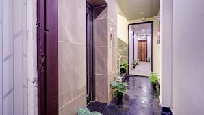 Um corredor com paredes de mármore, porta de madeira e plantas em vasos.