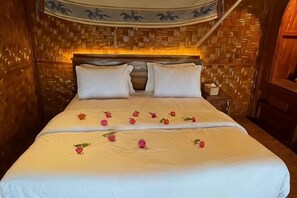 Cama com lençóis brancos, duas almofadas e pétalas de rosas espalhadas.