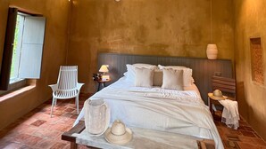 Quarto com cama, cadeira, mesa de cabeceira, abajur e janela.