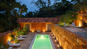 Piscina retangular com espreguiçadeiras e um muro de pedra ao redor.