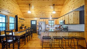 Interior de uma cabana de madeira com área de jantar, cozinha e banquetas de bar.