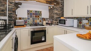 Uma cozinha compacta com parede de pedra, painel de azulejos, micro-ondas, forno e torradeira.