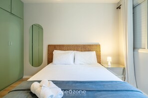 Quarto bem arrumado com cama, mesa de cabeceira, guarda-roupa verde e espelho fixado na parede.