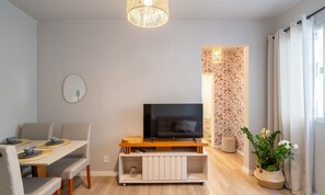 Uma sala de estar moderna com televisão de tela plana, uma área de jantar com mesa e cadeiras, e uma planta decorativa.
