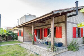 Uma casa com fachada de tijolos, persianas vermelhas e uma rede na frente.