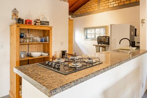 Cozinha com bancada de granito, fogão a gás, geladeira e janela com persianas.