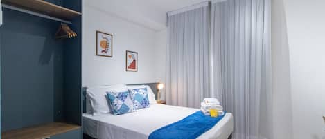 Quarto de hotel com cama, mesa de cabeceira, guarda-roupa e janela com cortinas.