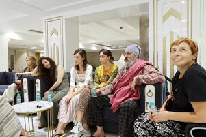 Um grupo de pessoas sentadas num sofá em um interior moderno com piso de mármore e paredes brancas.