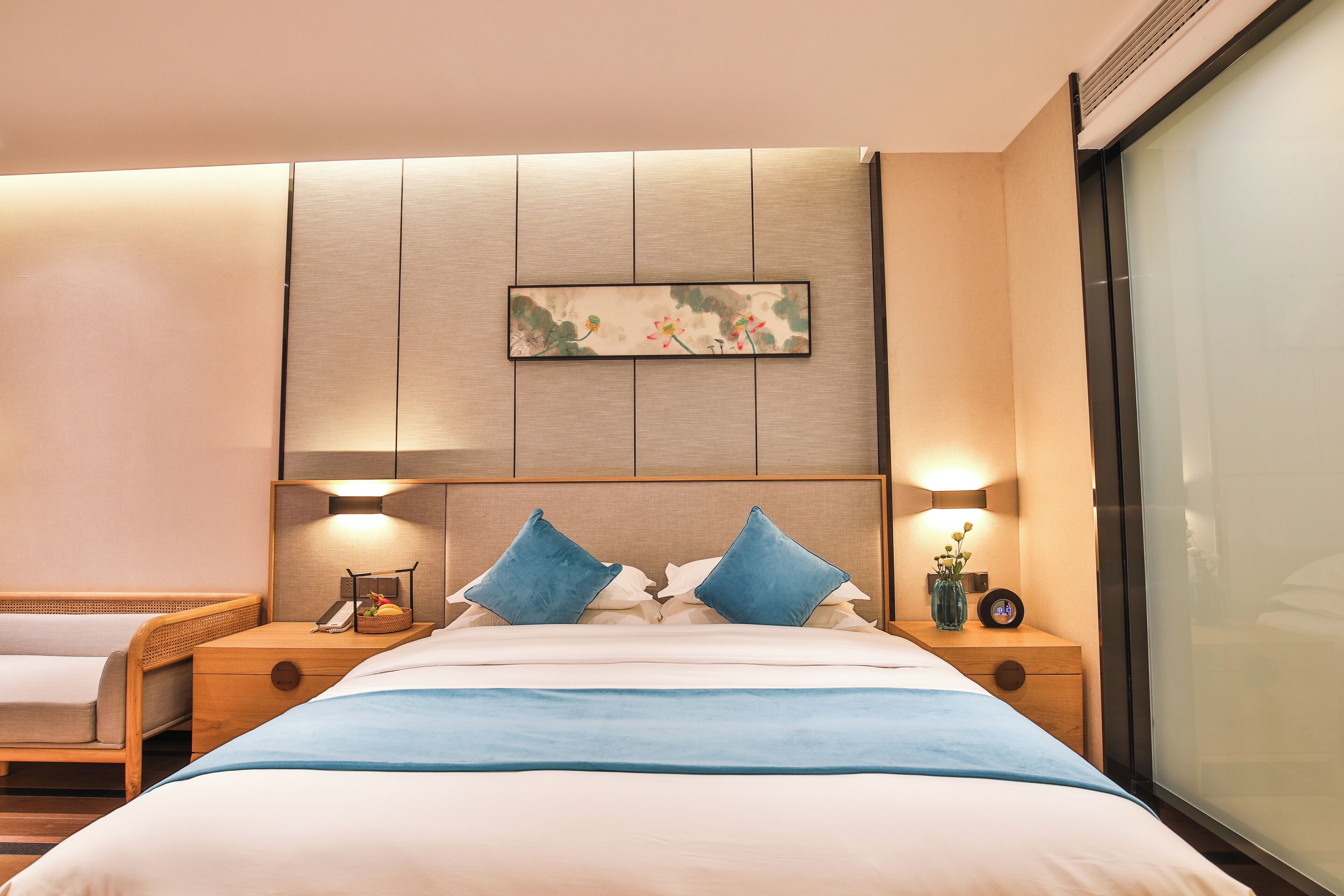 Quarto de hotel com uma cama grande, duas mesas de cabeceira, um criado-mudo, uma obra de arte pendurada na parede e uma janela ampla.