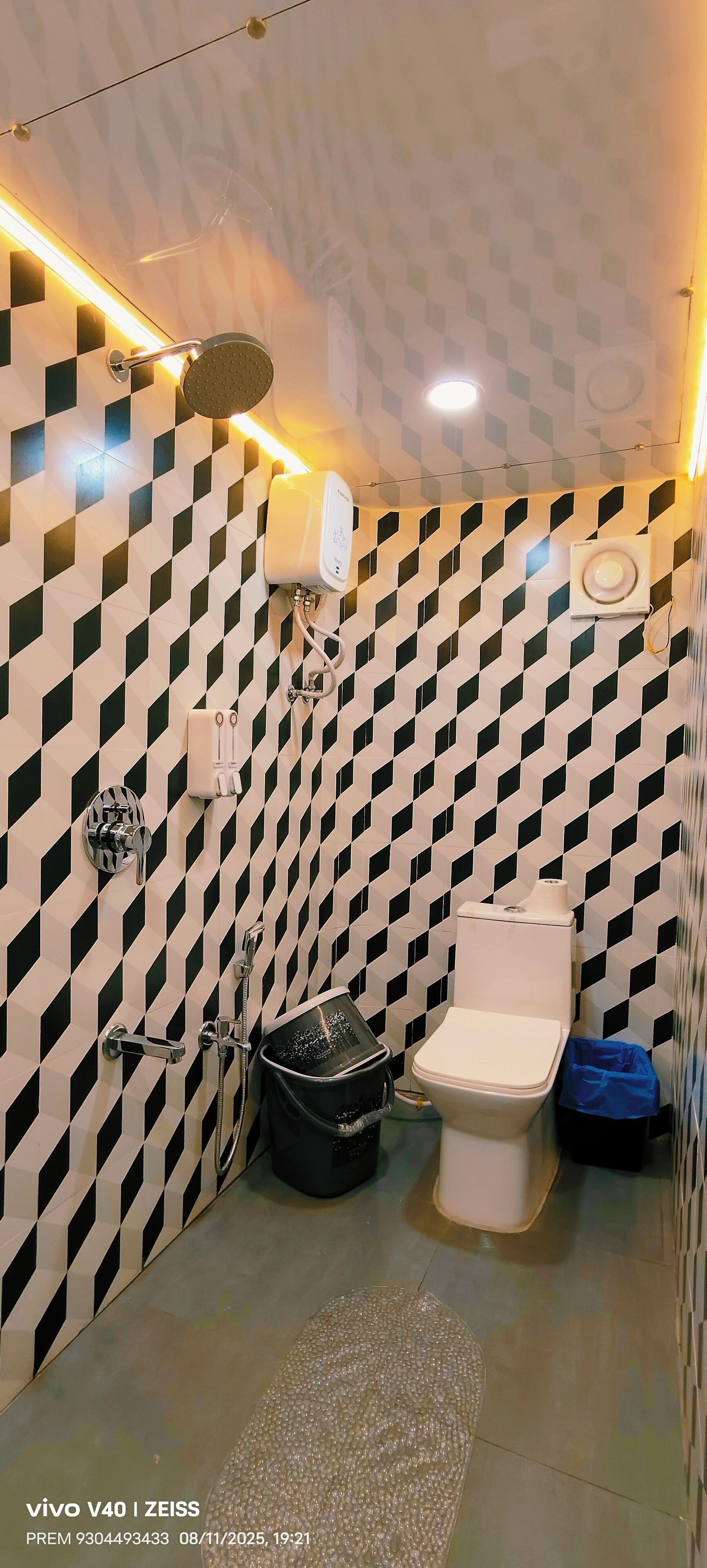 Um banheiro compacto com padrão quadriculado preto e branco, vaso sanitário, bidê, chuveiro e lixeira.