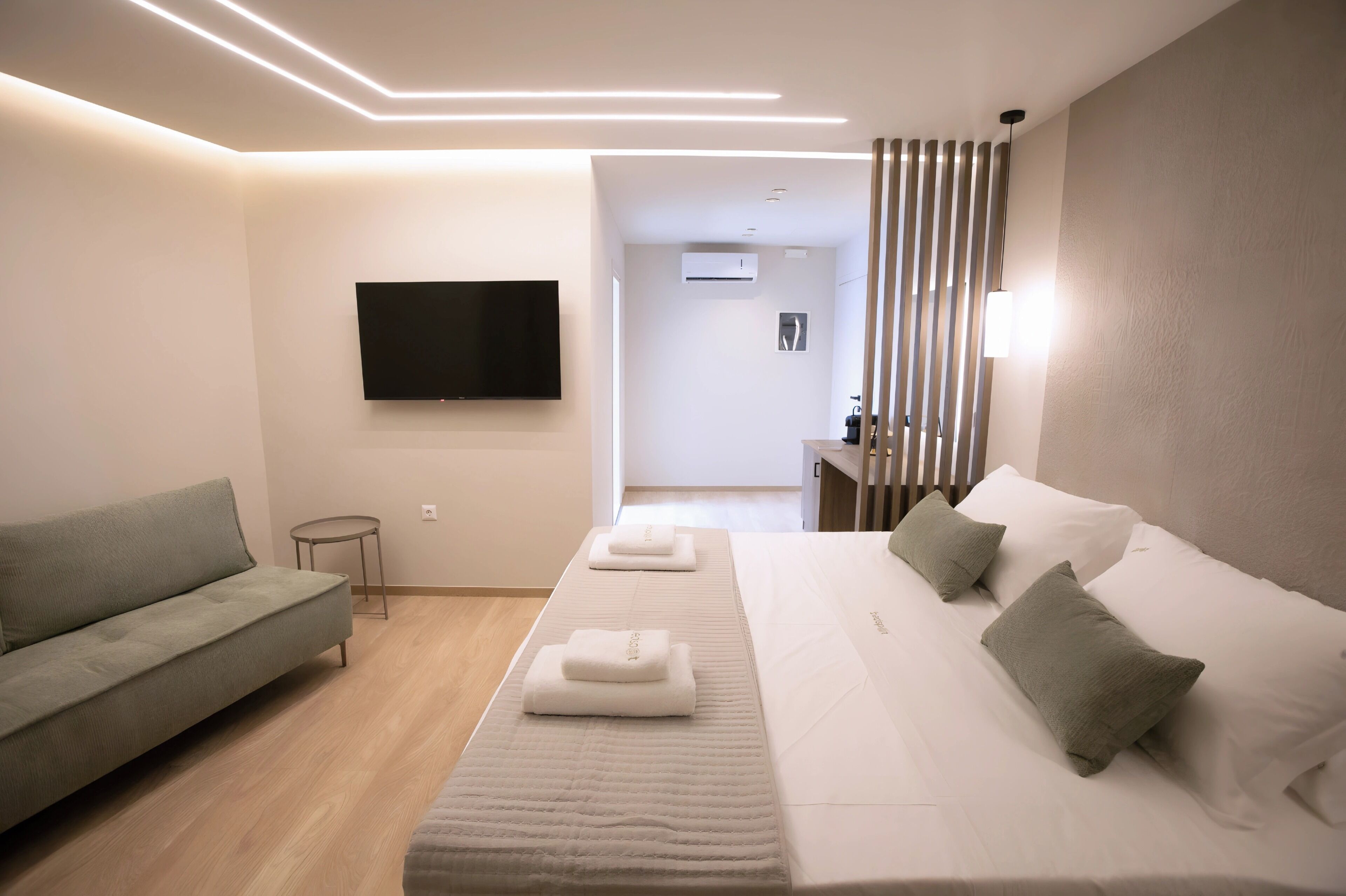 Quarto de hotel moderno com uma cama, um sofá, uma TV e uma pequena mesa.