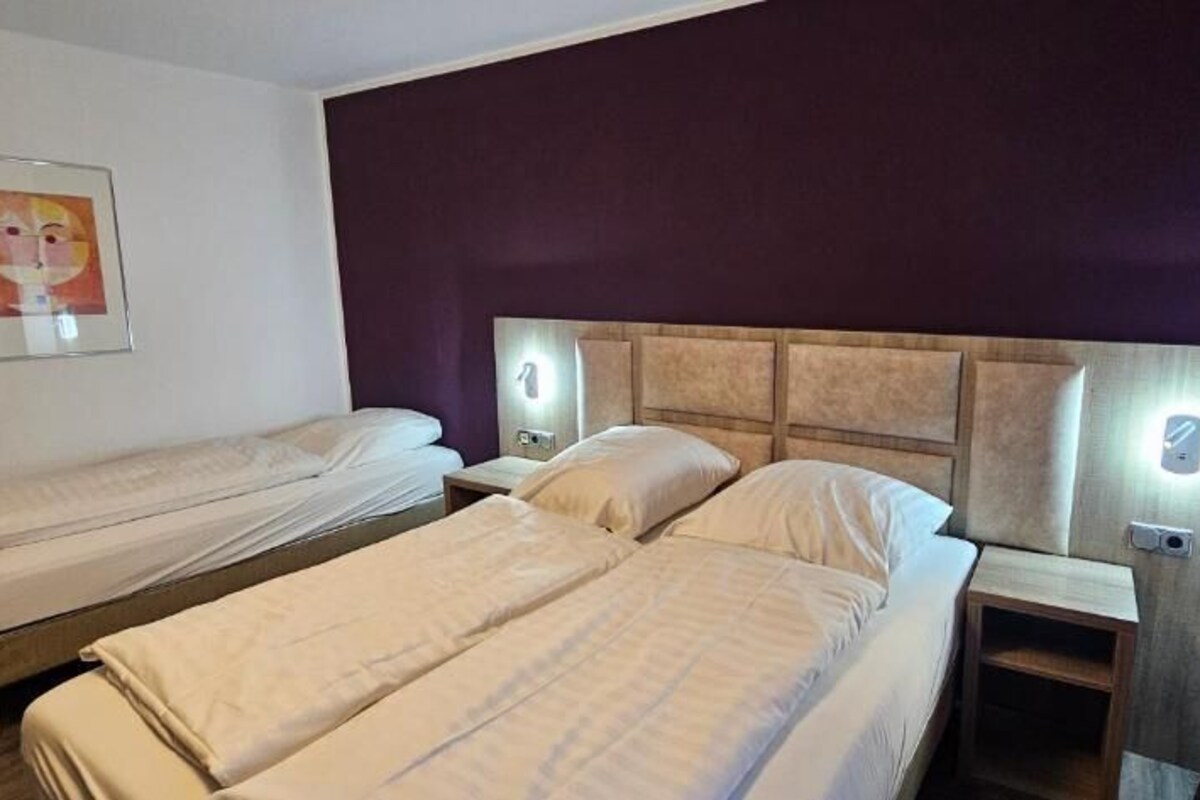 Quarto de hotel com duas camas de solteiro, uma mesa de cabeceira com abajur e uma obra de arte pendurada na parede.