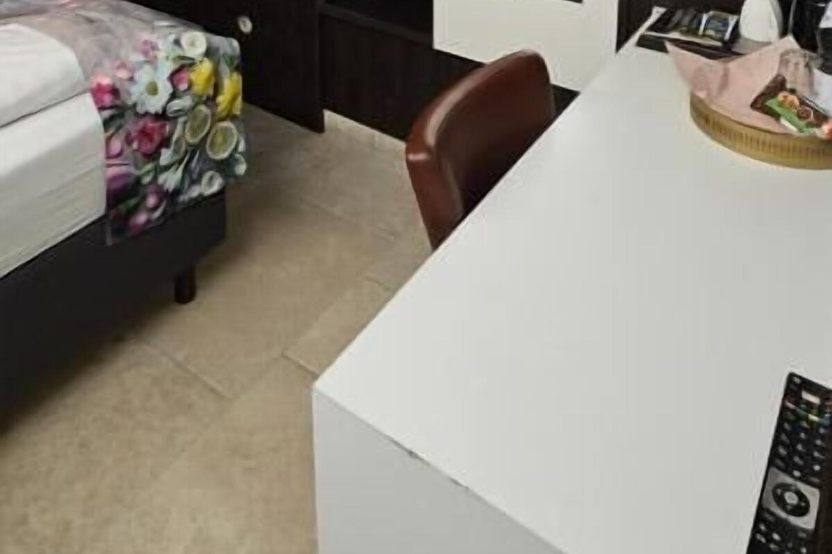 Quarto de hotel com cama, escrivaninha, cadeira, espelho e guarda-roupa.