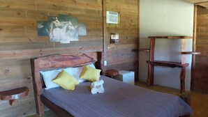 Quarto de cabana de madeira com cama, duas almofadas, luminária na parede e uma cadeira de madeira.