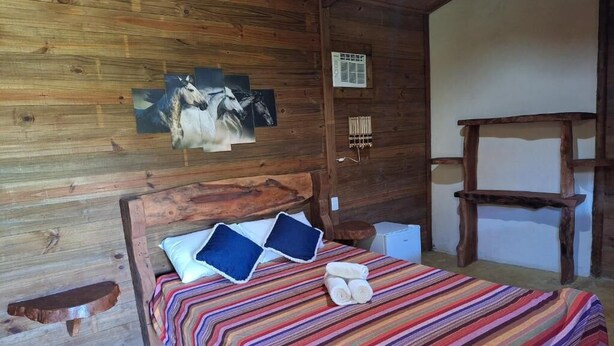 Quarto de cabana de madeira com cama, uma cadeira e um quadro de cavalos na parede.