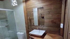 Uma casa de banho de madeira com cabine de duche em vidro, sanita branca e toucador de madeira com espelho.