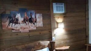 Um quarto de madeira com uma cama, almofadas, um quadro, uma mesa e uma cadeira.
