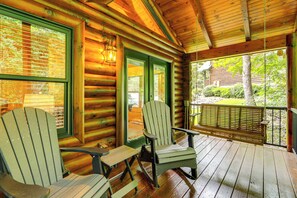 Uma cabana de madeira com varanda, duas cadeiras Adirondack e um banco.
