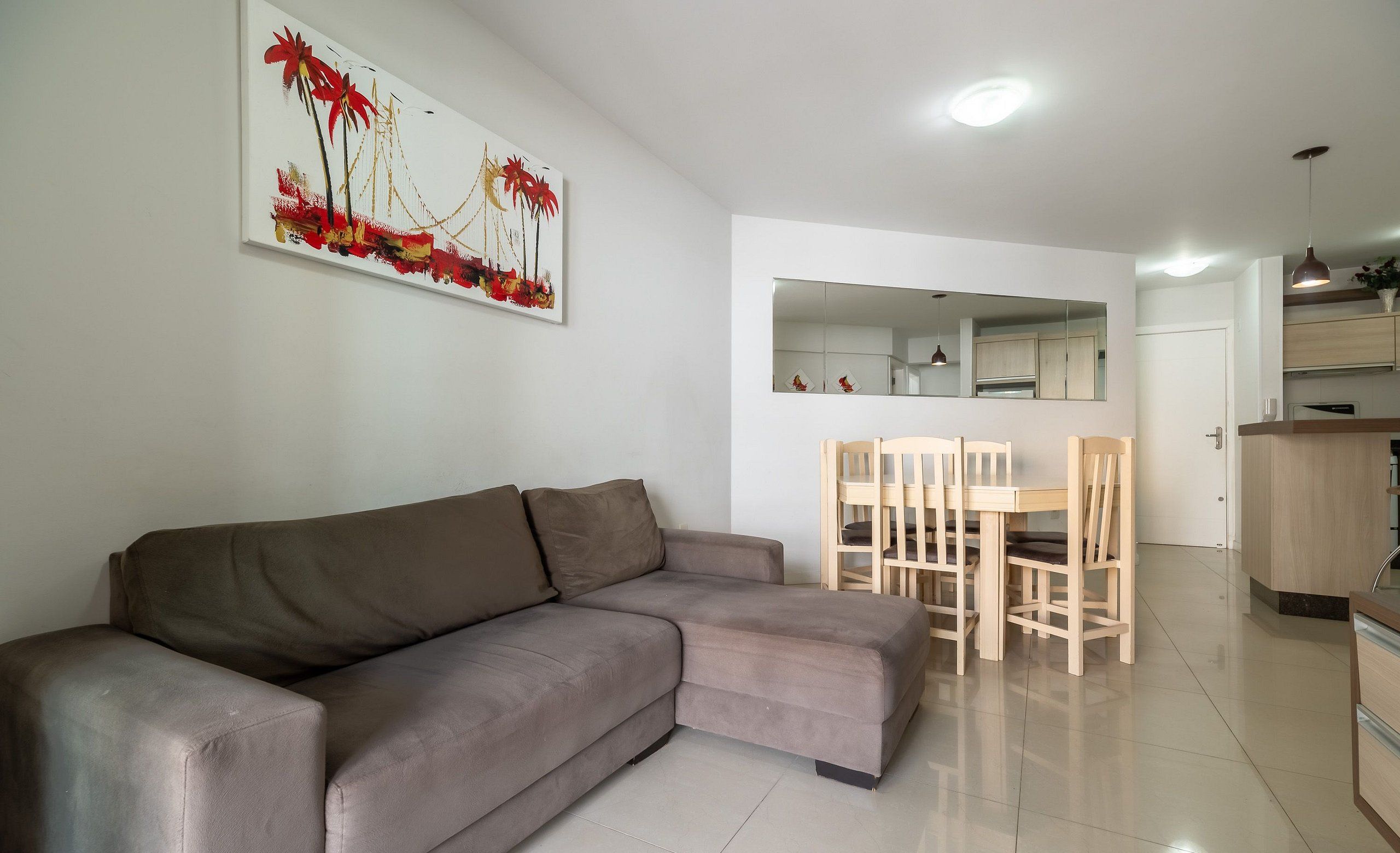 Uma sala de estar moderna com um sofá seccional cinza, uma área de jantar com cadeiras de madeira, uma cozinha com armários de madeira e um espelho grande na parede.