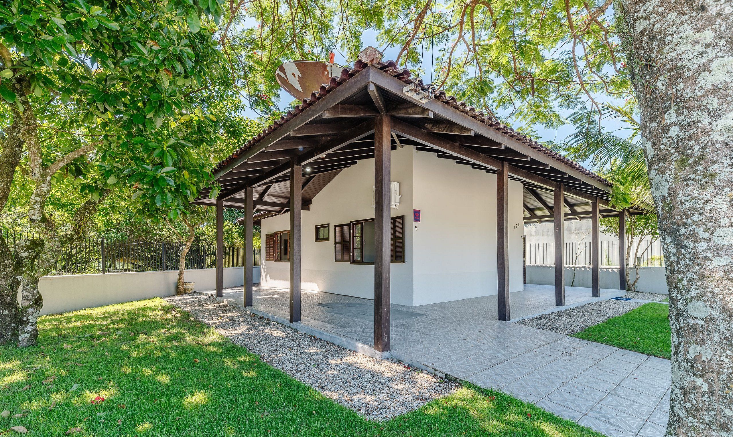 Uma área externa coberta com estrutura de pérgola, parede branca e placa com o número 126.