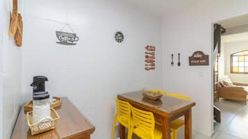 Uma sala de jantar com uma mesa de madeira, cadeiras amarelas, uma cafeteira e uma cesta sobre a mesa.