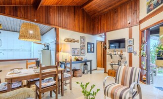 Uma sala de estar acolhedora com móveis de madeira, uma mesa de jantar e uma TV fixada na parede.