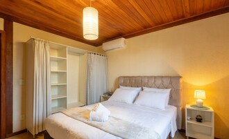 Quarto com cama, mesa de cabeceira, luminária, ar condicionado e guarda-roupa.