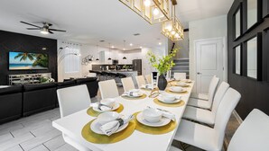 Uma sala de jantar moderna com uma mesa comprida posta para seis pessoas, cadeiras brancas e um ventilador de teto.