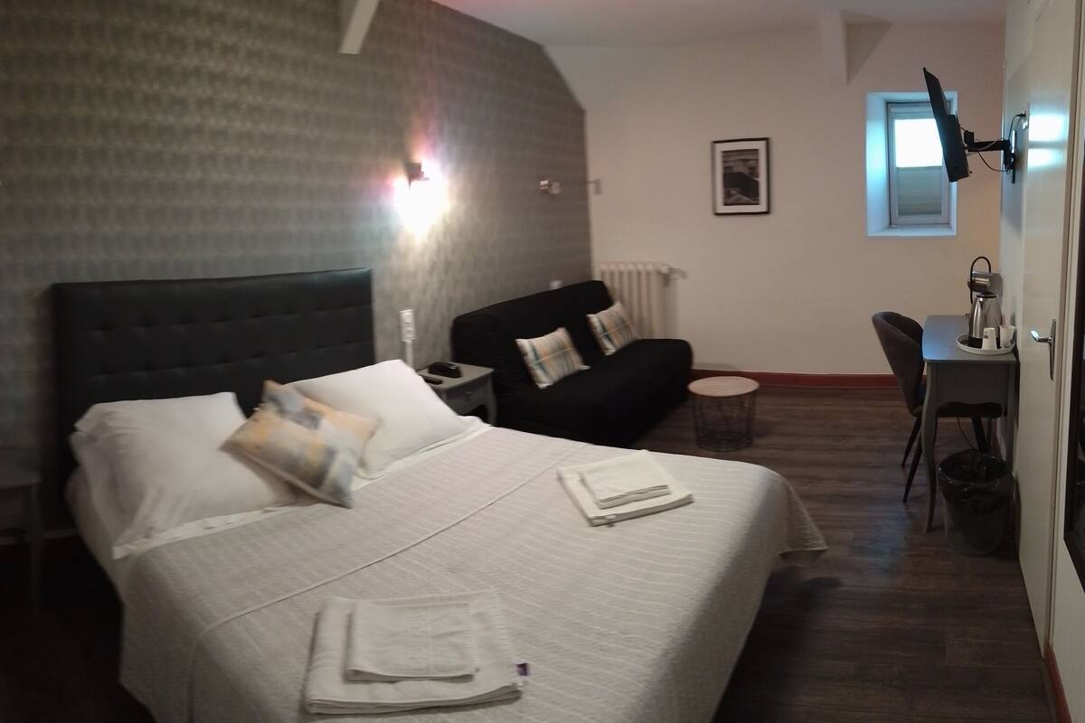 Quarto de hotel com uma cama grande, uma escrivaninha, uma cadeira e um radiador.