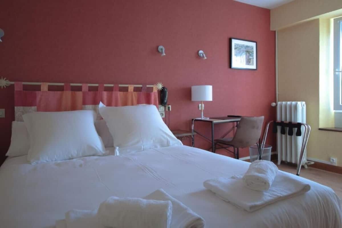 Quarto de hotel com uma cama grande, uma escrivaninha, uma cadeira e um radiador.