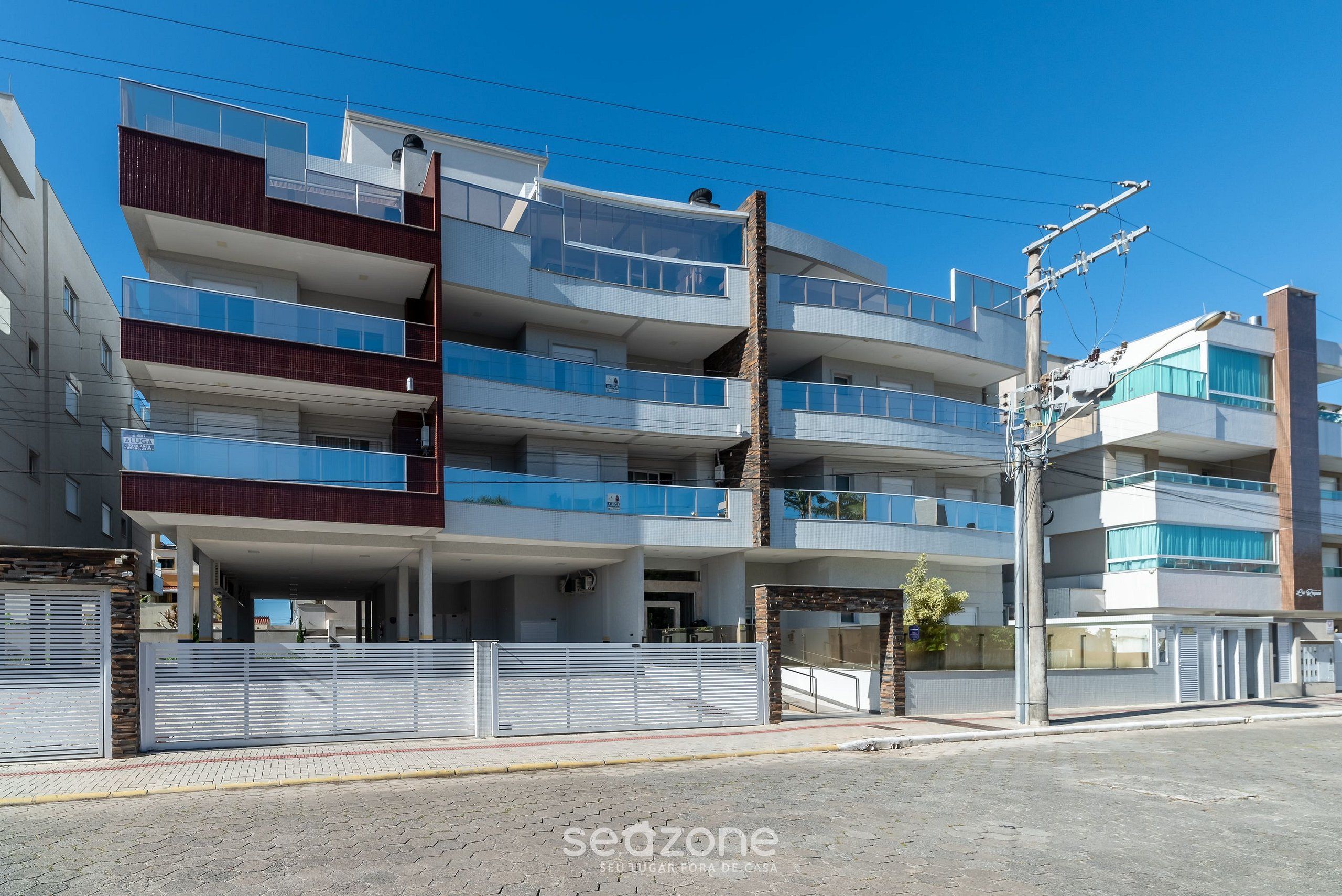 Um edifício residencial com vários andares, varandas, portão fechado e céu azul claro.
