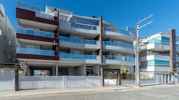 Um edifício residencial com vários andares, varandas, portão fechado e céu azul claro.