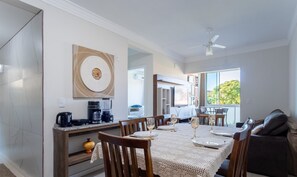 Uma área de refeições com uma mesa posta para quatro pessoas, uma cafeteira e vista para o exterior.