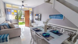 Sala de estar moderna com sofá, mesa de jantar e cadeiras. Há uma televisão na parede e uma janela com cortinas.