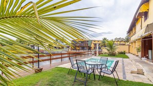 Uma área de piscina com mesa e cadeiras de vidro, cercada por um deck de madeira e um gramado.
