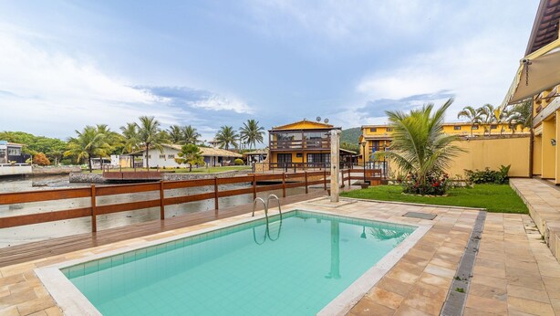 Piscina com deck de madeira, rodeada por palmeiras e edifícios com fachadas amarelas e castanhas.