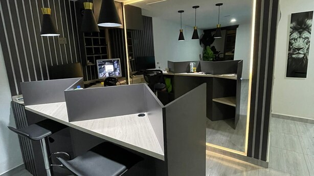 Um espaço de escritório moderno, com cubículos, uma área central de mesas e iluminação pendente.
