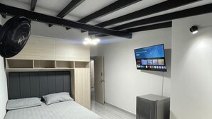 Quarto moderno com cama, televisão na parede, ventilador e um pequeno armário.