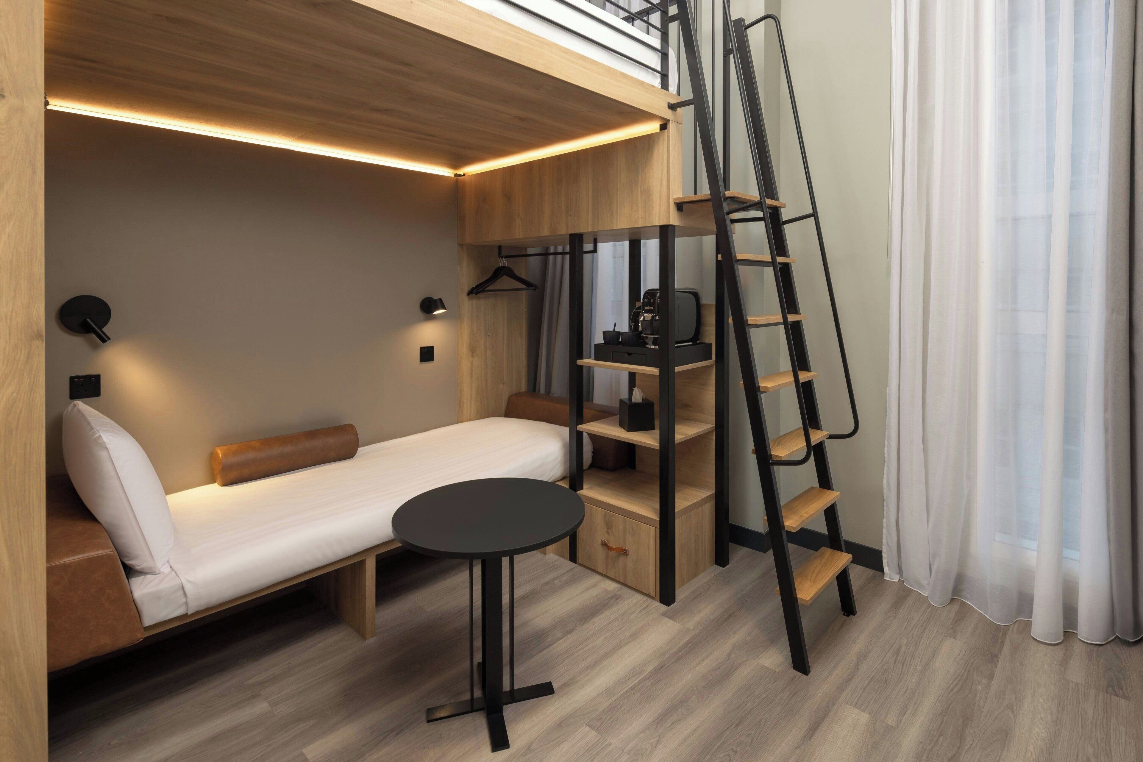 Quarto compacto com cama, uma mesinha, escada e cabideiro.