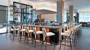 Uma área de bar moderna com um balcão comprido, vários bancos e uma variedade de garrafas e copos.